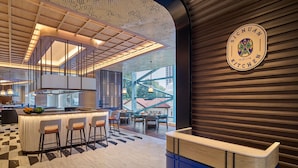 Cozinha moderna com ilha central, banquetas e vista para uma ponte através de amplas janelas.