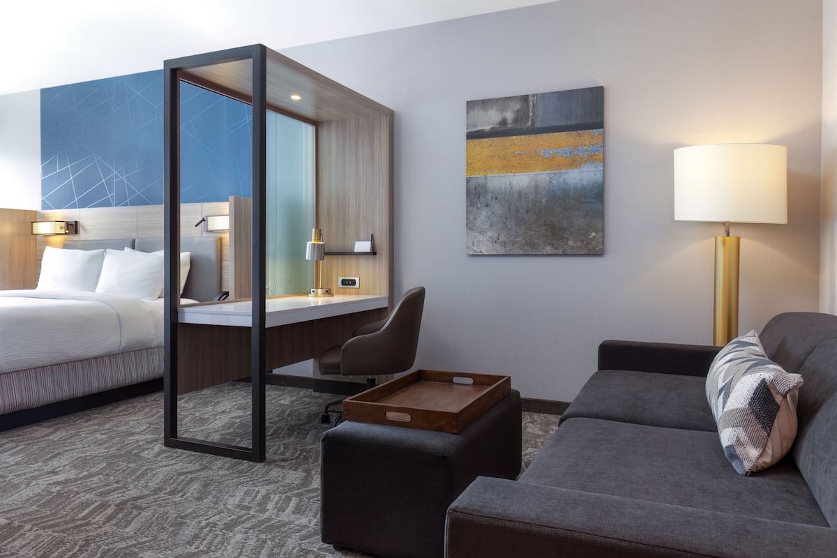 Quarto de hotel com cama, escrivaninha, sofá e uma pequena mesa.