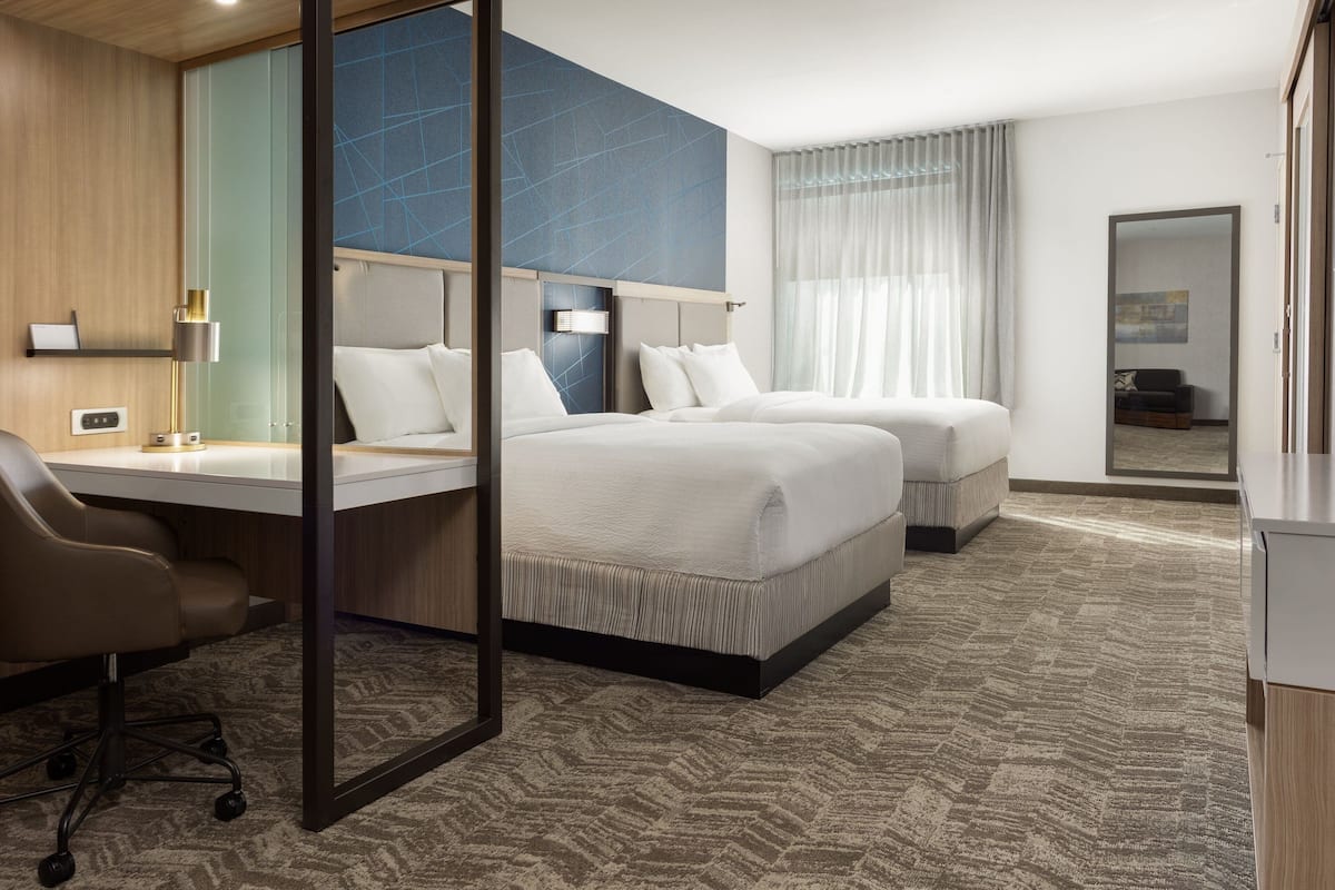 Quarto de hotel com duas camas, uma escrivaninha, uma cadeira e um espelho grande.