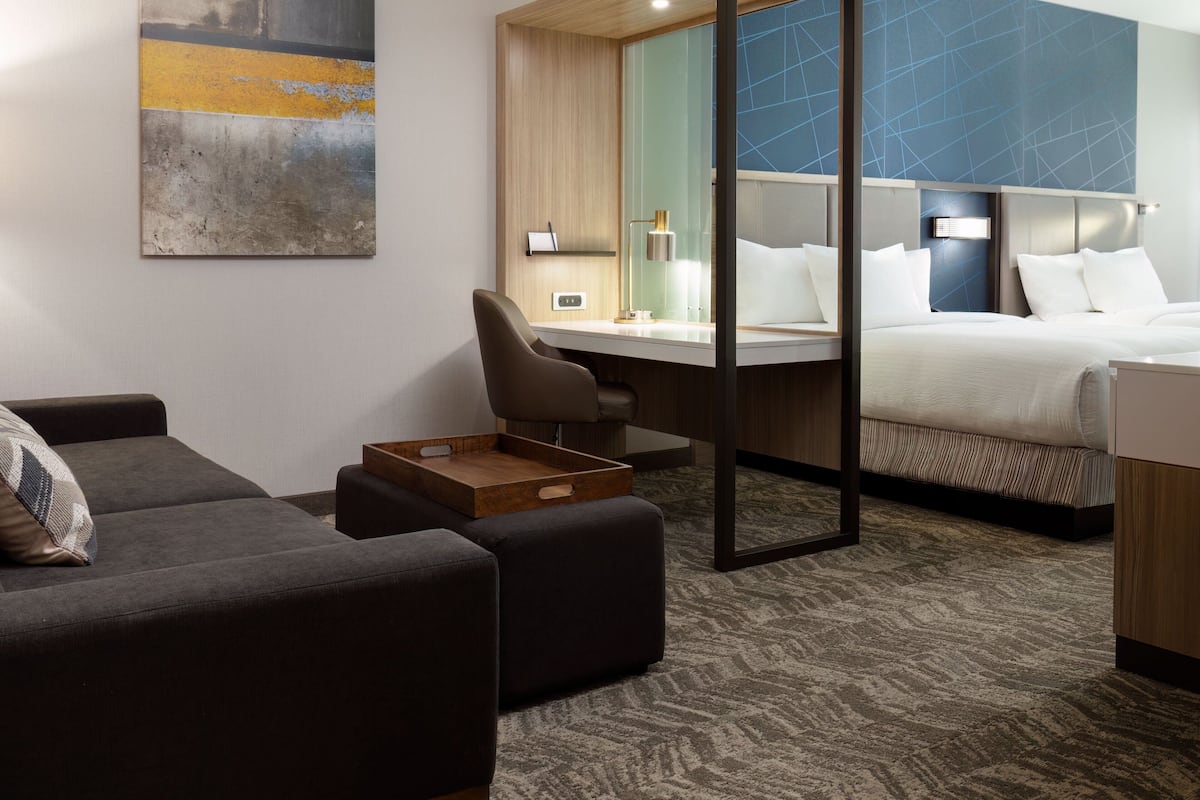 Quarto de hotel com cama, escrivaninha, poltrona, sofá e um grande quadro abstrato na parede.