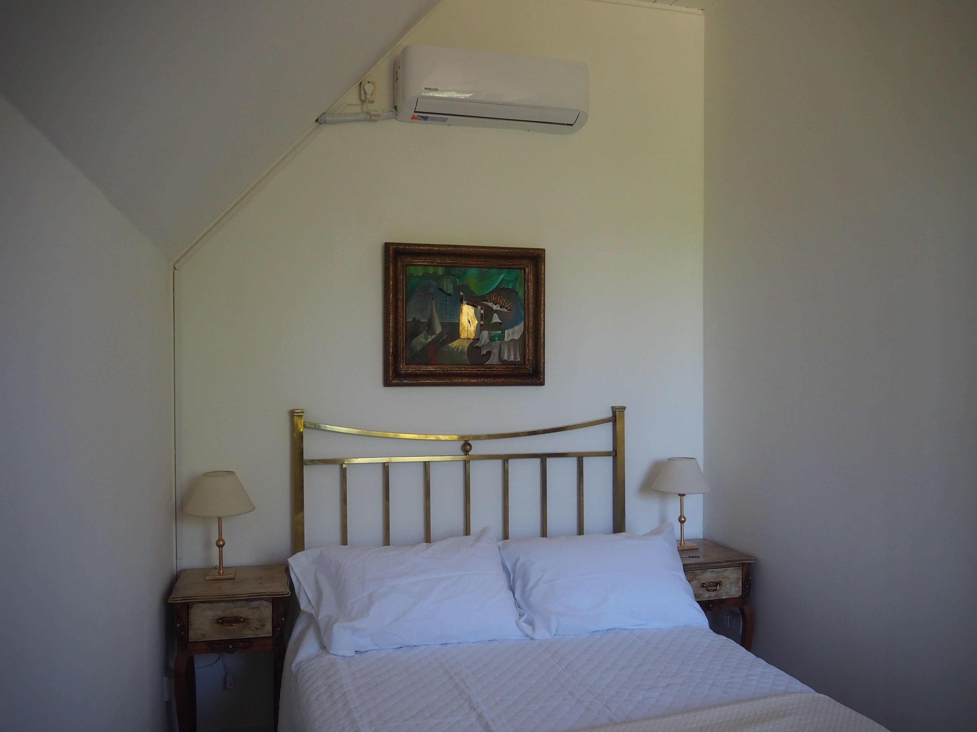 Quarto com cama, duas mesas de cabeceira, ar-condicionado fixado na parede e um quadro emoldurado.
