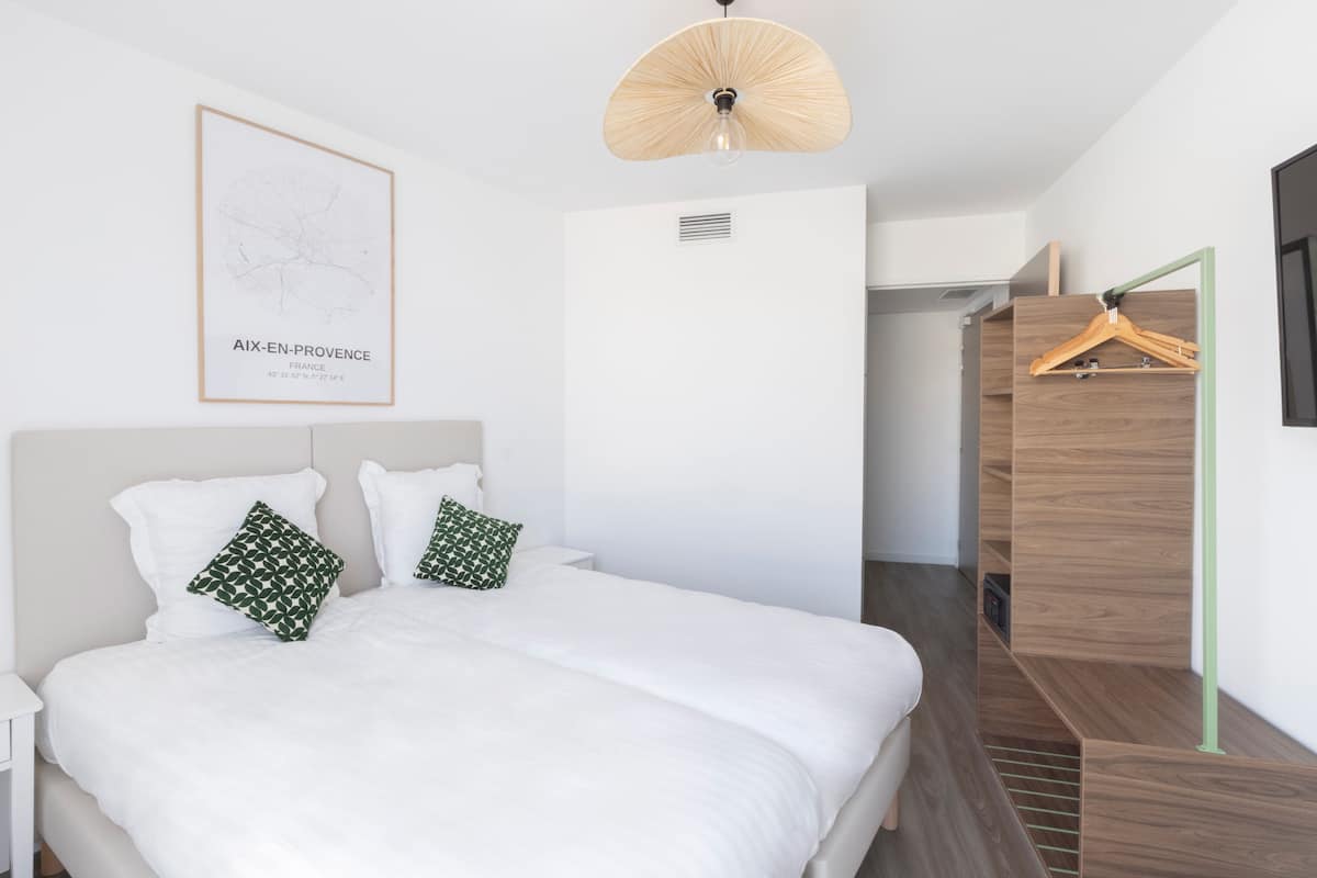 Quarto de hotel moderno com uma cama grande, luminária pendente, guarda-roupa de madeira e um mapa emoldurado na parede.