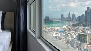 Quarto de hotel com uma janela grande que oferece vista para a cidade, uma cama e uma cortina.