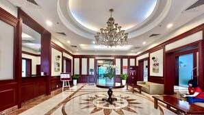 Um hall amplo com um lustre central, piso de mármore e um balcão de recepção.