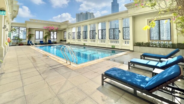 Piscina com espreguiçadeiras, vista para o horizonte da cidade e um edifício com a placa 'LET'.