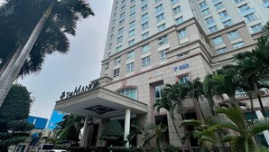 Um hotel moderno de muitos andares, com um acesso principal destacado, uma área coberta e uma placa com a inscrição 'The Manor'.