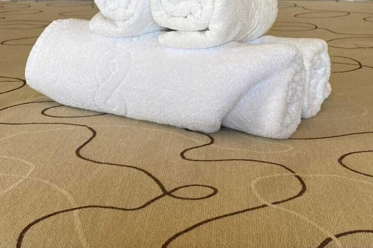 Uma cama bem arrumada com toalhas brancas dobradas e um pequeno buquê de flores cor-de-rosa em cima.
