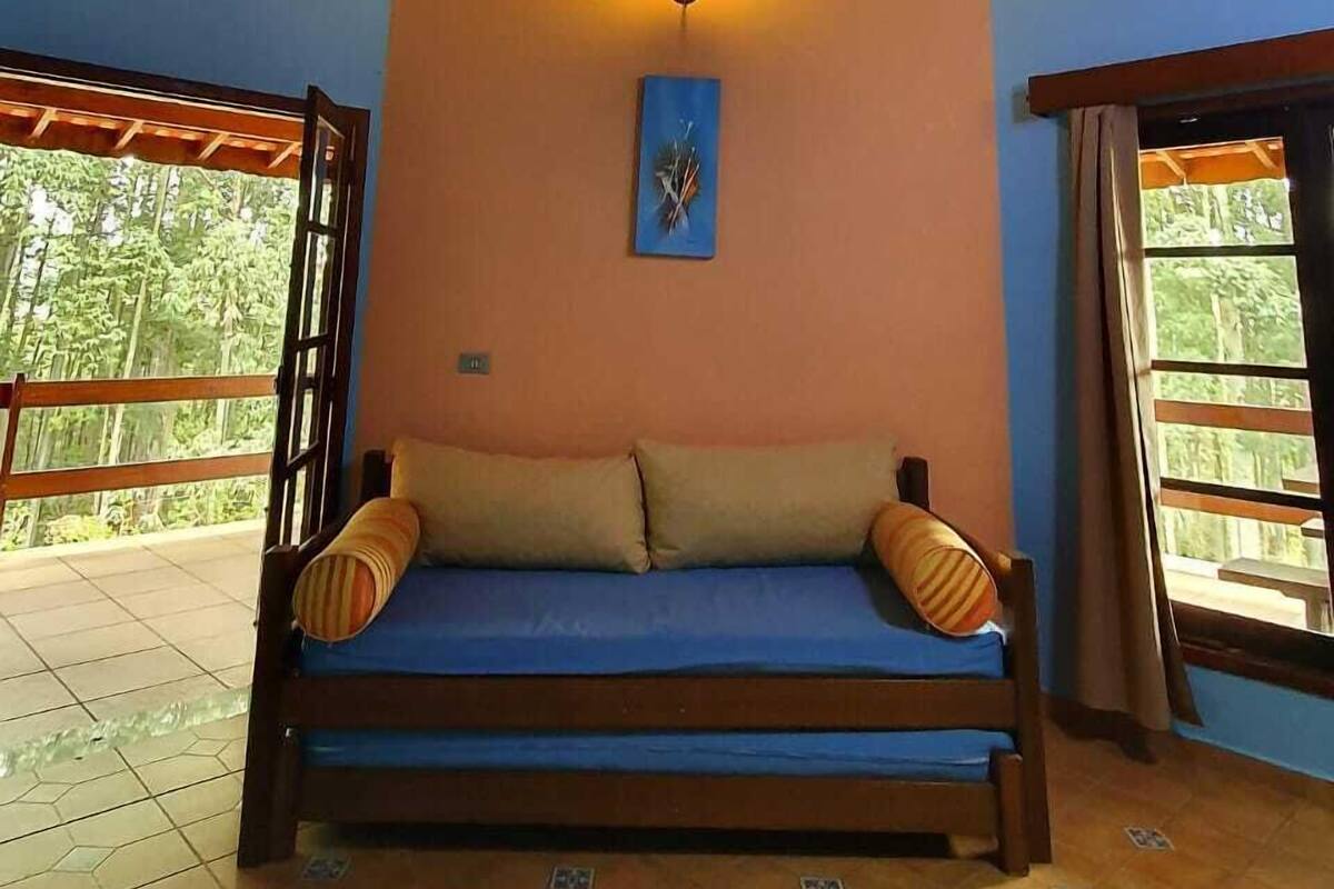 Quarto com cama, luminária na parede e janela com vista para árvores.