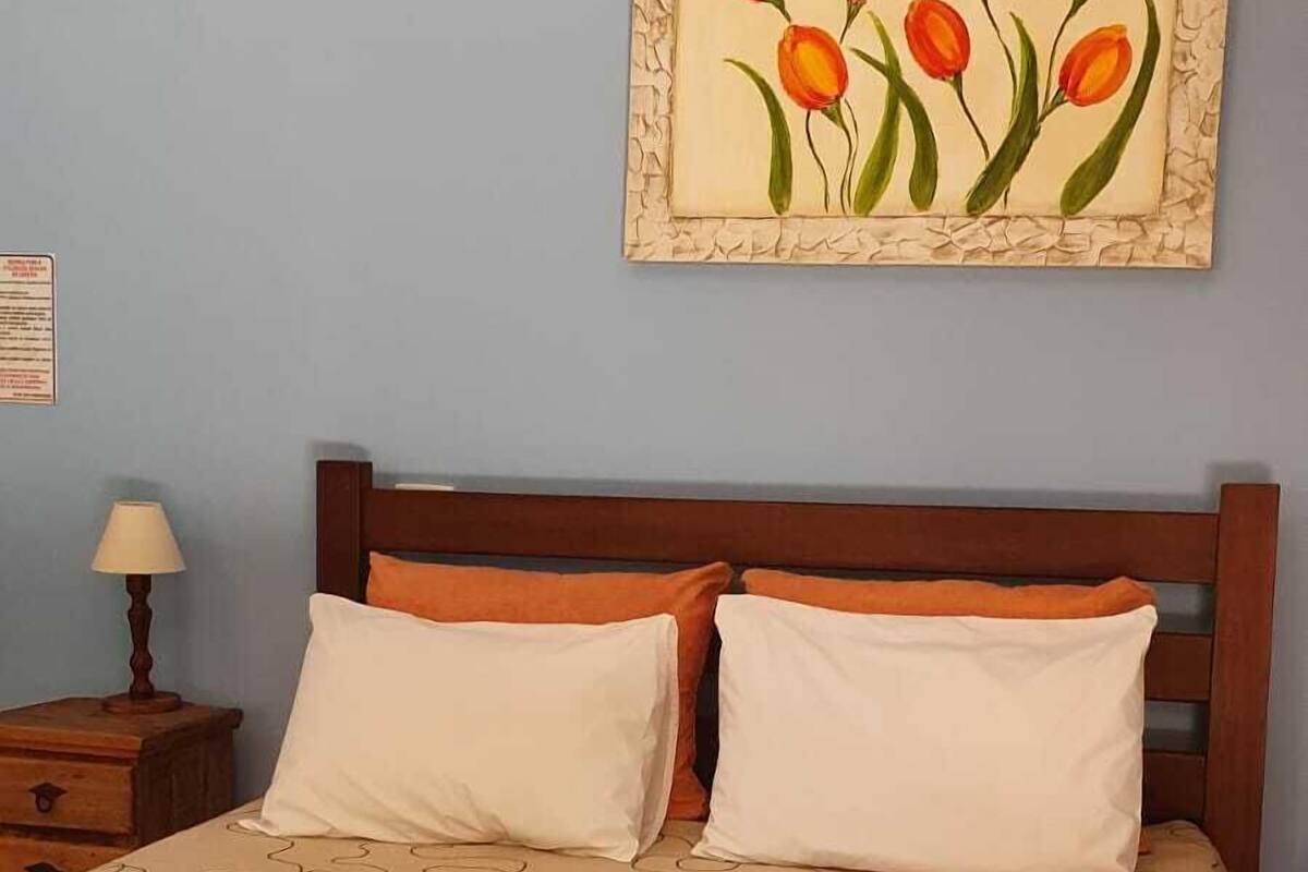 Uma cama bem arrumada com colcha estampada, dois travesseiros e um quadro com flores de tulipa na parede.