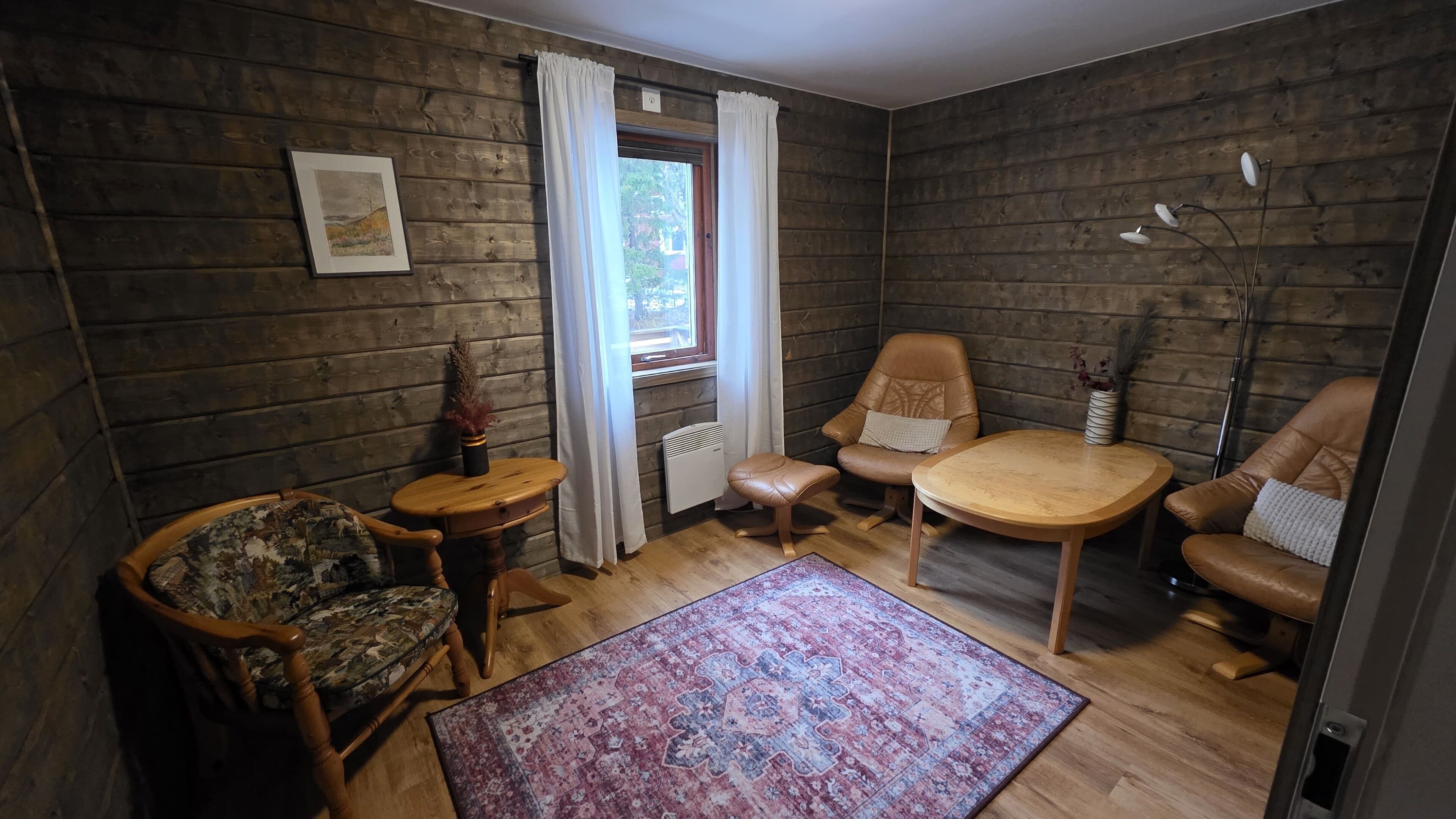 Um quarto acolhedor com paredes de madeira, uma janela com cortinas, um tapete estampado e poltronas de couro.
