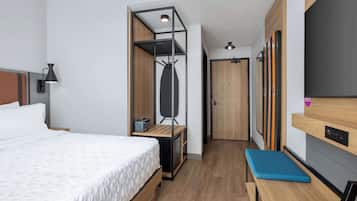 Quarto de hotel moderno com cama, escrivaninha, banco, cabideiro e guarda-roupa.