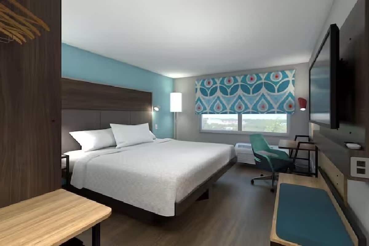 Quarto de hotel com cama, escrivaninha, cadeira, televisão e janela com vista.