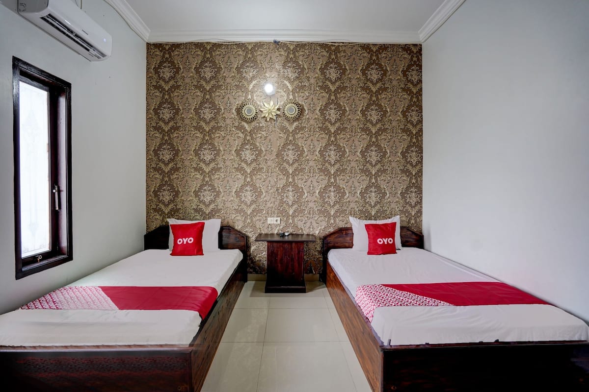 Quarto de hotel com duas camas de solteiro, uma mesa de cabeceira de madeira, ar-condicionado fixado na parede e papel de parede estampado.