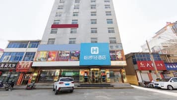 Hotel com placa azul chamativa, vários andares e área de estacionamento à frente.