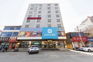 Hotel com placa azul chamativa, vários andares e área de estacionamento à frente.