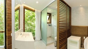 Casa de banho moderna com chuveiro em cabine de vidro, lavatório branco e toucador de madeira.
