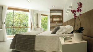 Quarto moderno com cama, mesas de cabeceira, guarda-roupa e varanda com vista para o verde.