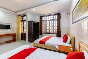 Quarto de hotel com duas camas, televisão, guarda-roupa e um banquinho.