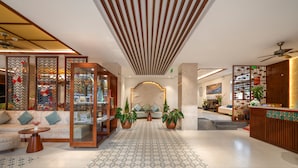 Um hall amplo com piso estampado, um balcão de recepção e uma área de estar com sofá e poltronas.