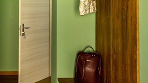Um quarto com um banco de madeira, um cabide suspenso, uma porta e uma mala.
