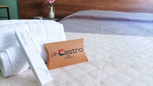 Uma cama bem arrumada com um edredom branco, uma caixa marrom com a inscrição "inCastro b&b Crotone" e uma toalha branca ao lado.