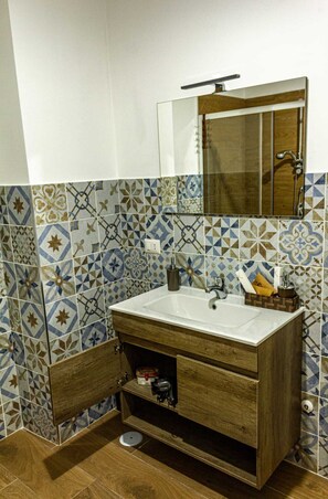 Casa de banho com toucador de madeira, pia branca e espelho em cima.