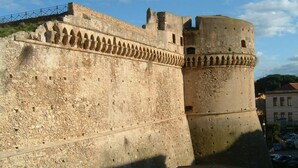 Um muro de pedra histórico com merlões e uma torre redonda, provavelmente parte de uma fortificação.