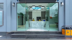 Entrada de um edifício moderno, com porta de vidro, balcão de recepção e uma luminária de teto diferenciada.