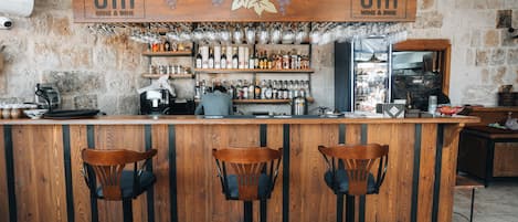 Uma área de bar com balcão de madeira, três banquetas e um letreiro com a inscrição 'vinho e gastronomia'.