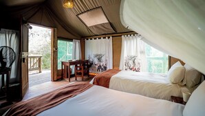 Quarto tipo tenda com duas camas, uma mesa e um ventilador.