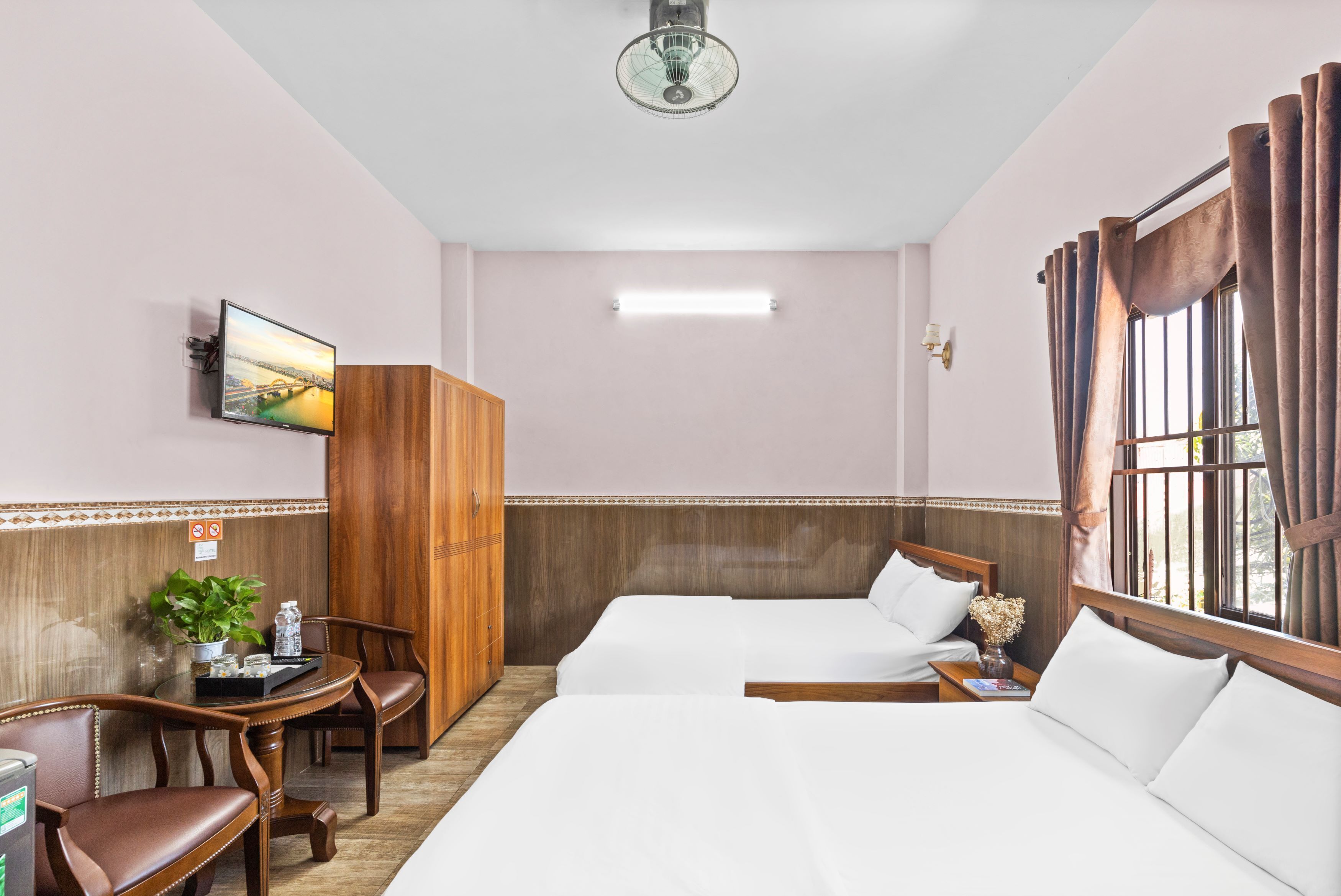 Quarto de hotel com duas camas, uma escrivaninha, uma cadeira, uma televisão e uma janela com cortinas.