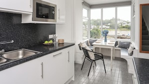 Cozinha moderna com armários brancos, bancada preta e micro-ondas embutido. Há uma janela com vista para casas e vegetação.