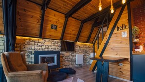 Um quarto acolhedor com lareira de pedra, vigas de madeira, um letreiro com a palavra 'hello' e uma área de estar confortável.