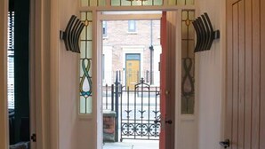 Um corredor com uma porta que dá para um pátio, um lustre pendurado e uma porta de vidro decorativa com padrões geométricos.