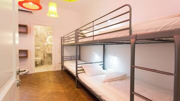 Quarto com beliches, piso de madeira, banheiro com pia e espelho, e porta que dá para outro cômodo.
