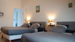 Quarto de hotel com duas camas, mesas de cabeceira com luminárias, uma porta e uma parede com um quadro emoldurado.