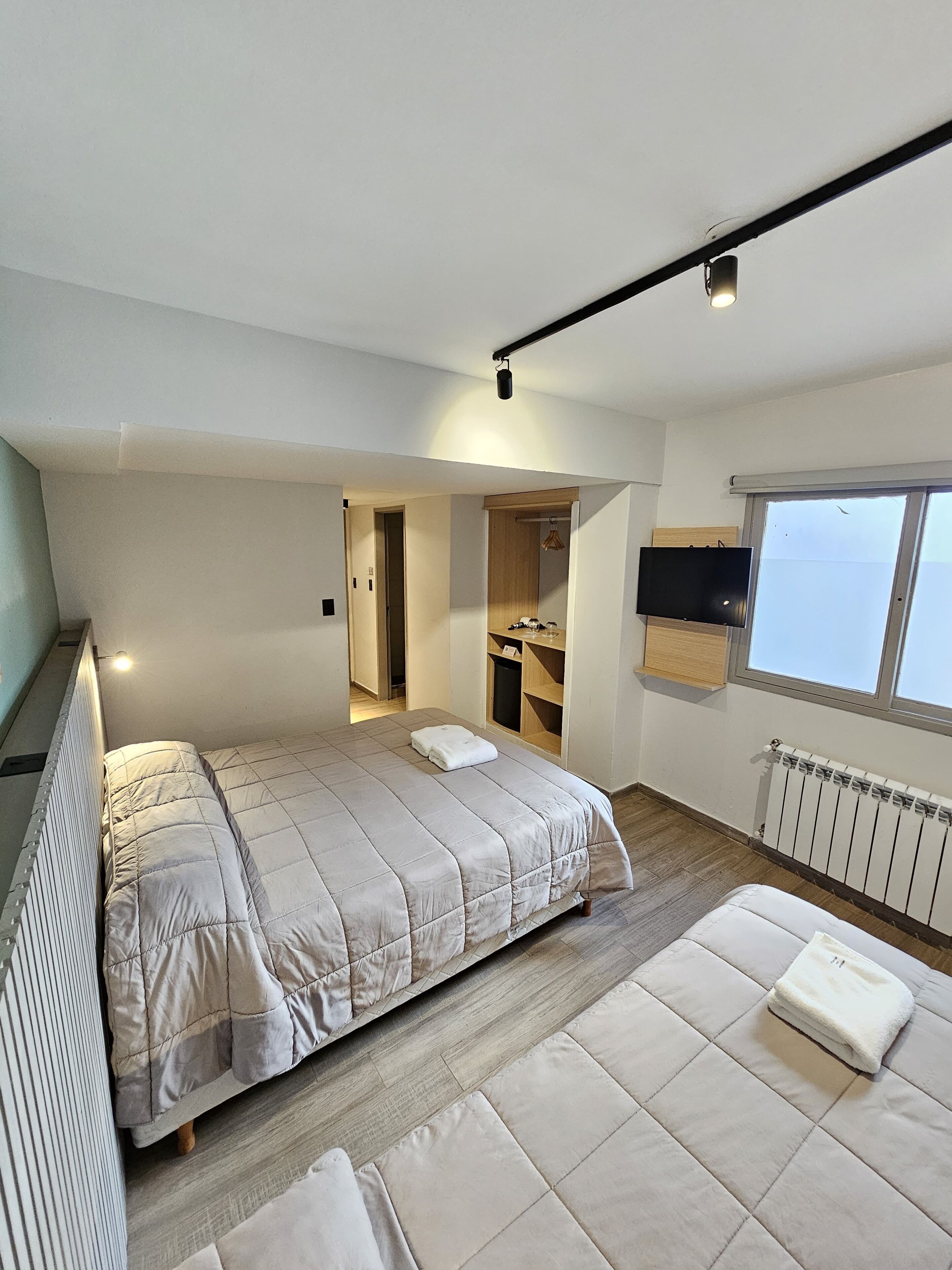 Quarto moderno com uma cama grande, um sofá menor, uma TV na parede e uma janela que oferece luz natural.