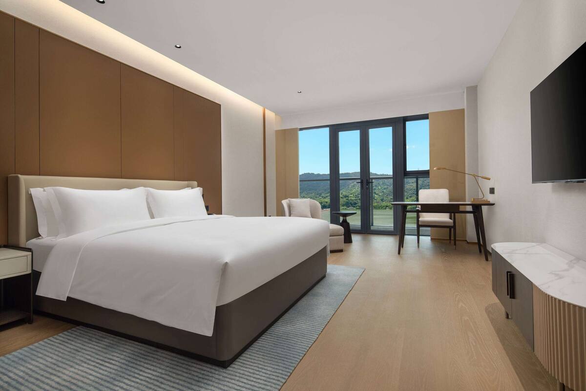 Quarto de hotel moderno com uma cama grande, uma escrivaninha e uma varanda com vista.