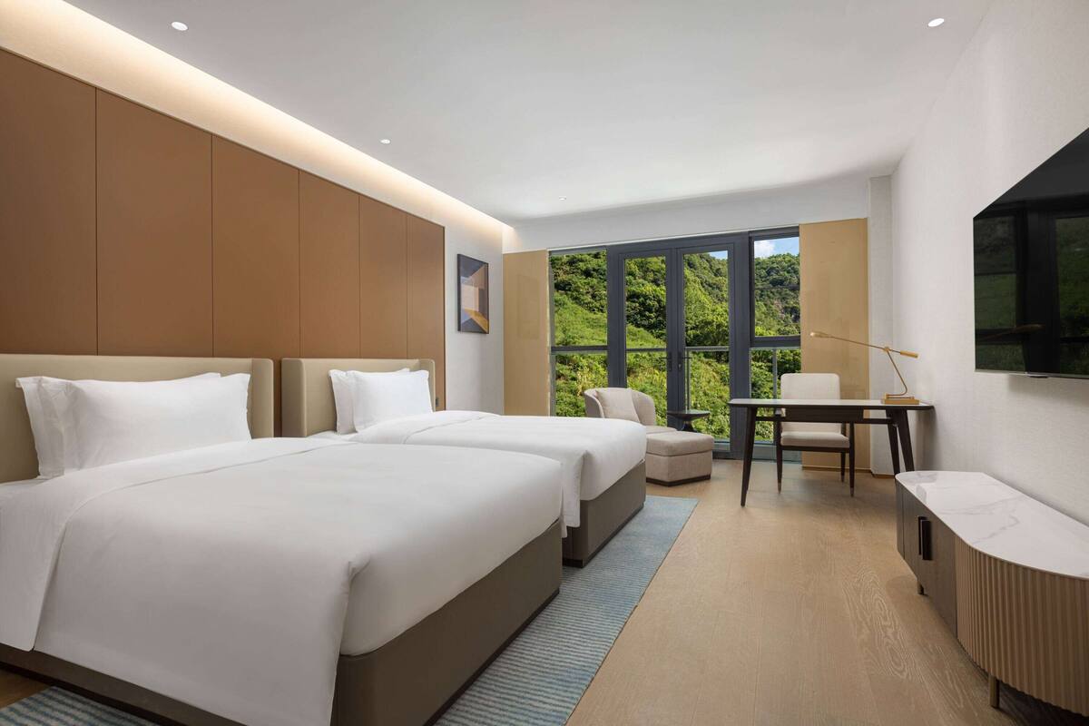Quarto de hotel moderno com uma cama grande, uma escrivaninha e vista para o verde.