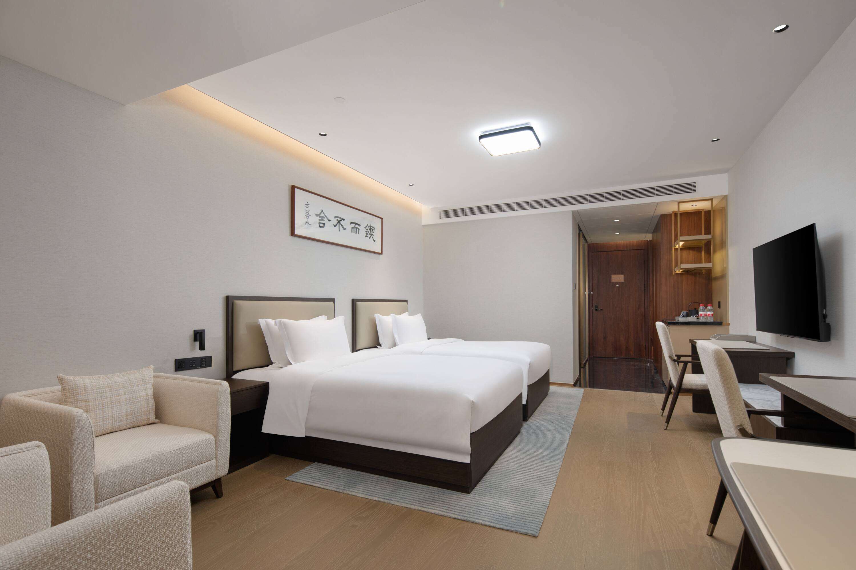 Quarto de hotel moderno com uma cama grande, um sofá, uma escrivaninha e uma televisão.