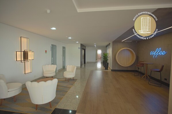 Um lobby moderno com um balcão de café, área de estar e mesa de recepção.