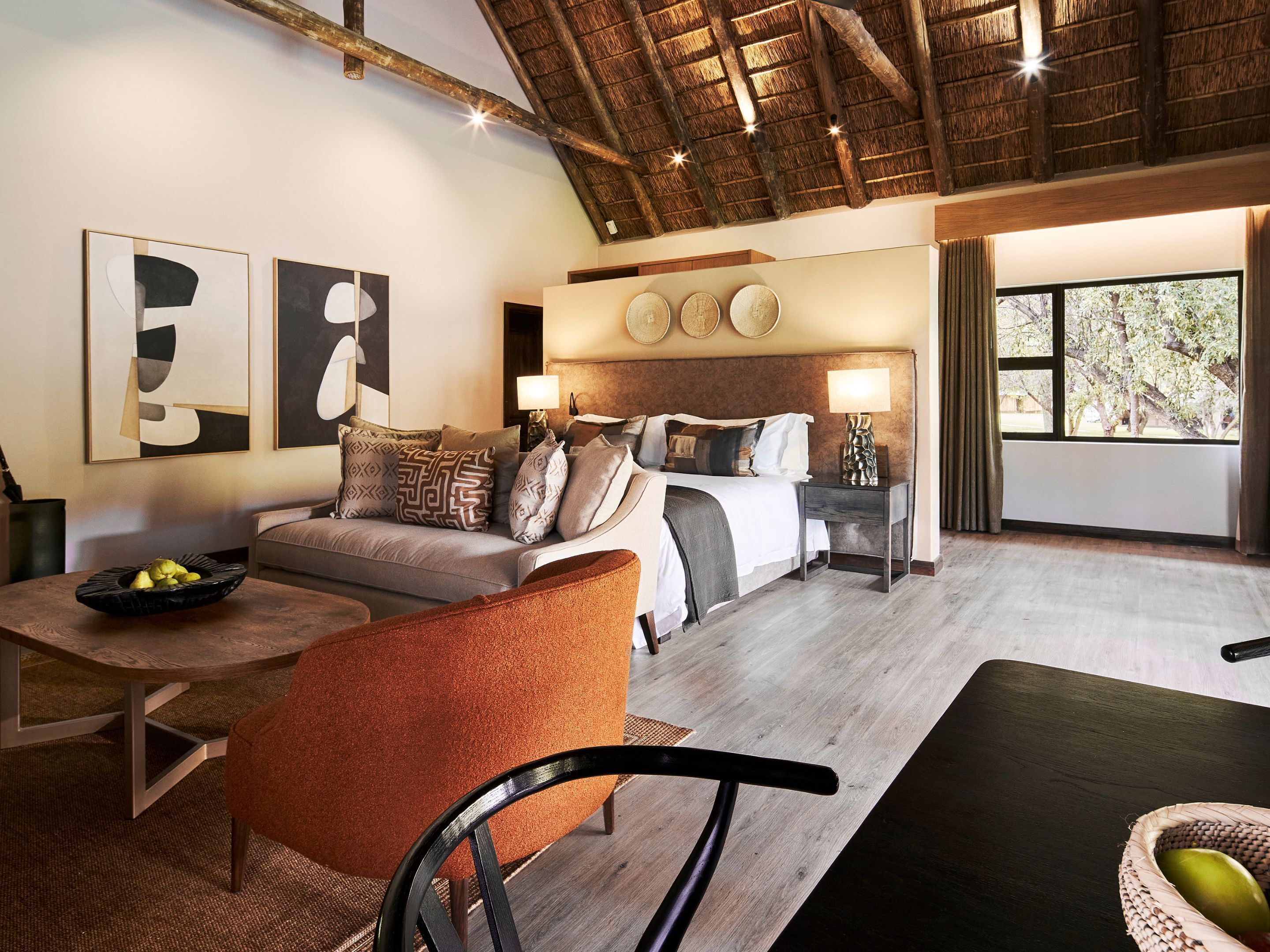 Quarto de hotel moderno com cama, sofá, mesa de jantar e uma janela grande.
