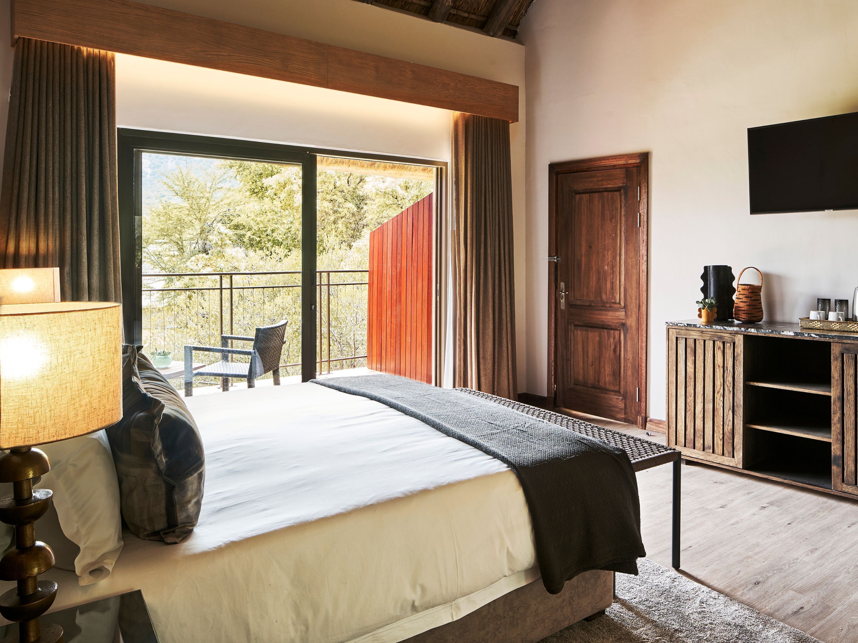 Quarto com cama, escrivaninha, cadeira e varanda com cortinas.