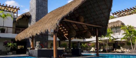 Uma área de piscina com estrutura de telhado de palha, espreguiçadeiras e um bar.