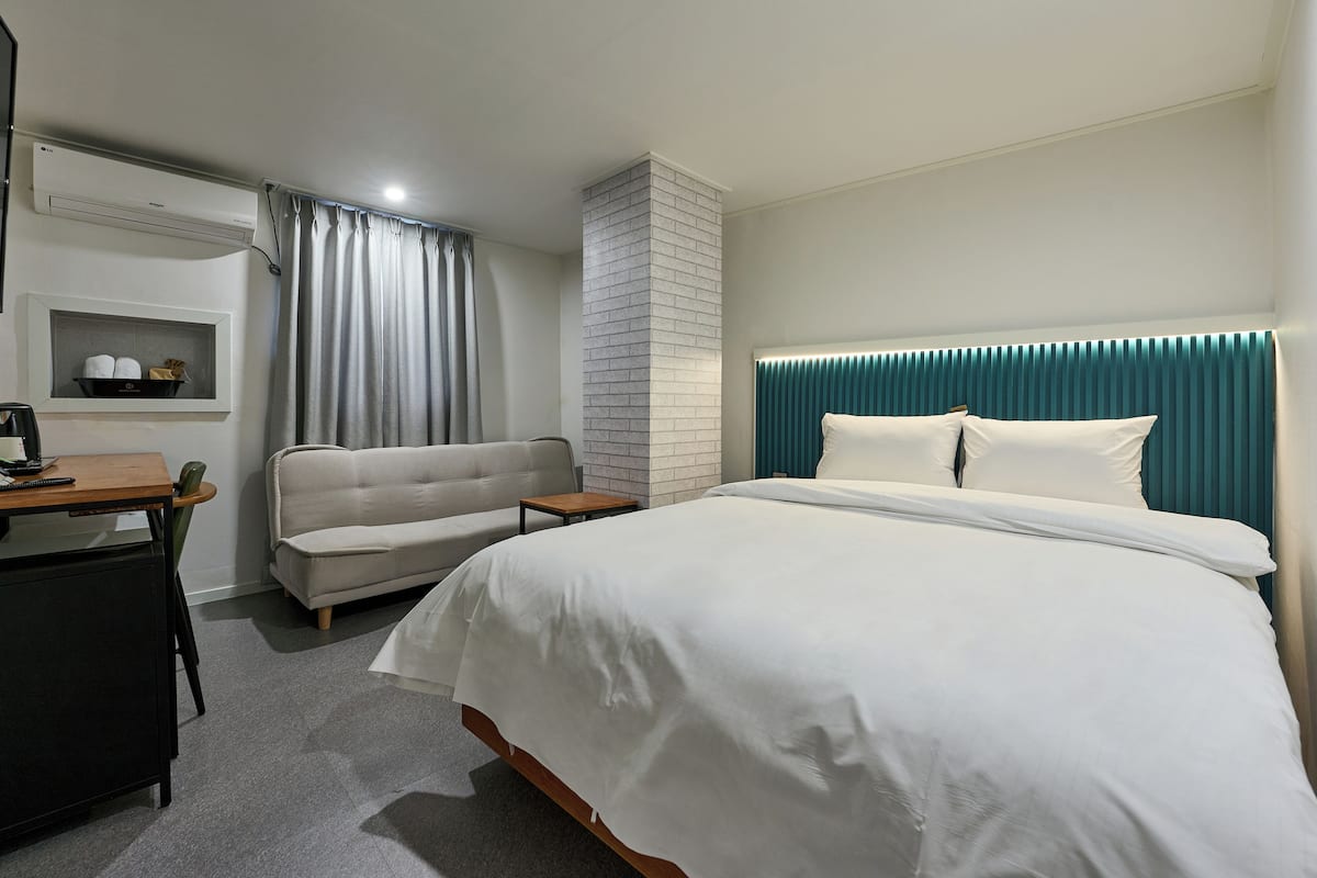 Quarto de hotel com cama, sofá, escrivaninha e uma pequena mesa.