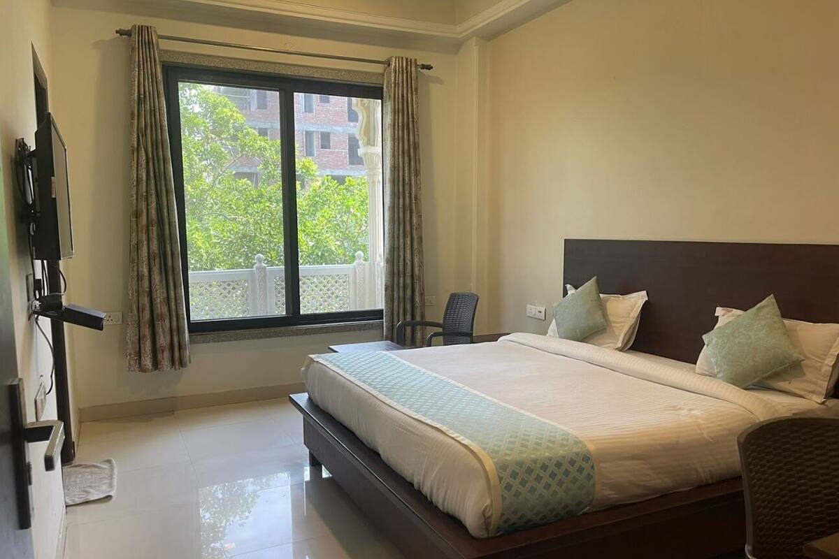 Quarto de hotel com uma cama grande, televisão, cadeira e janela com cortinas.