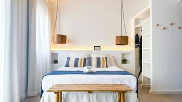 Um quarto com cama, mesas de cabeceira, um banco de madeira e um lustre.