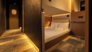Quarto de hotel com cama, cabeceira de madeira, mesinha de cabeceira e luminária fixada na parede.