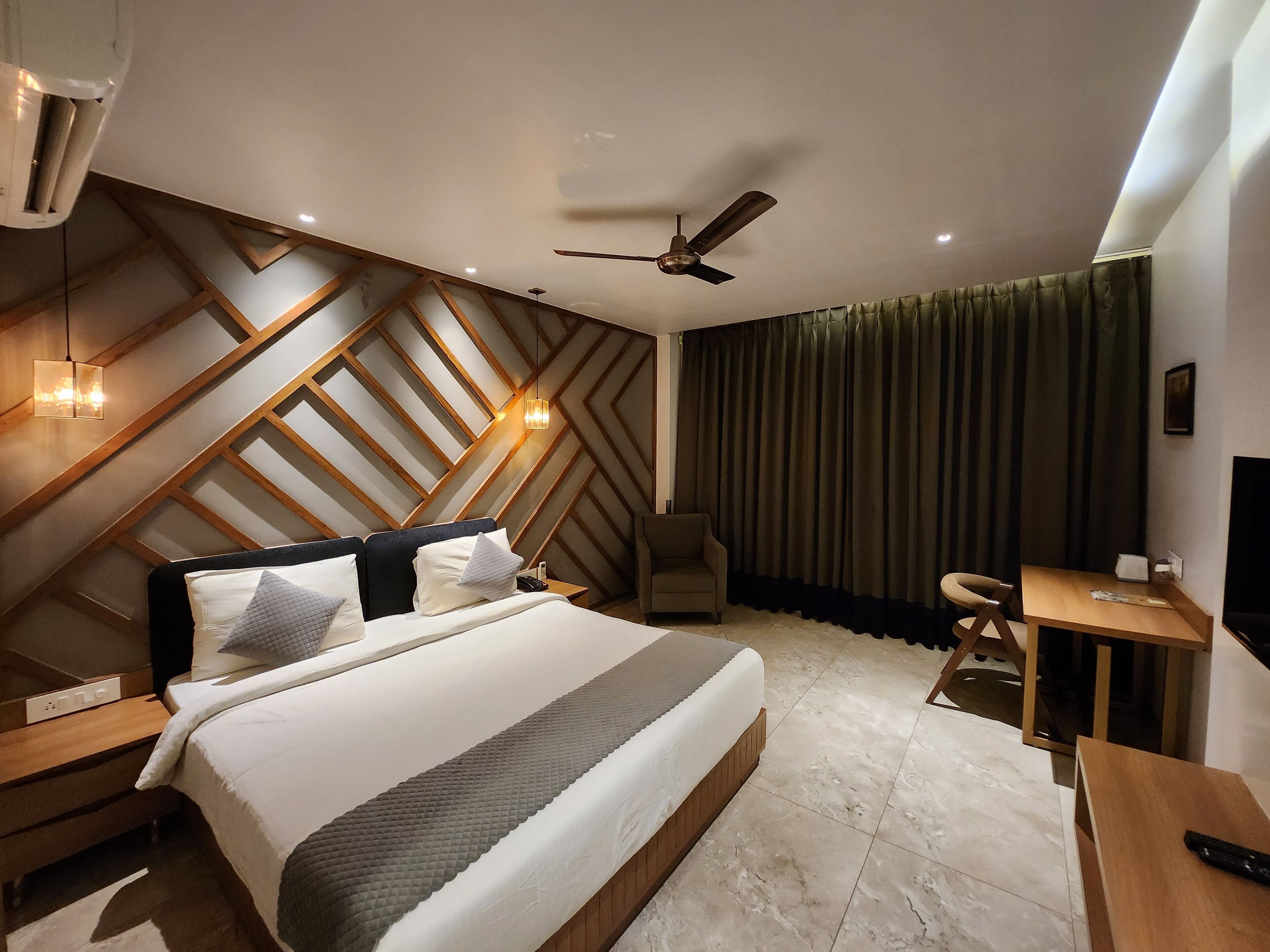 Quarto de hotel moderno com cama, escrivaninha, cadeira, ventilador de teto e televisão.