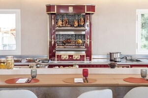 Cozinha com máquina de café expresso embutida, mesa de jantar posta com jogos americanos e janela com vista para árvores.
